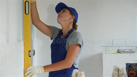 Young Woman Worker In The Uniform Uses A Spirit Level On The Bathroom Wall During Renovation