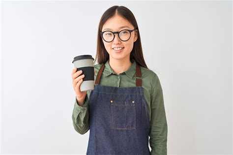 중국 바리스타 여성은 고립 된 흰색 배경 위에 커피를 마시는 앞치마 안경을 쓰고 행복한 얼굴을 하고 치아를 보여주는 자신감있는 미소로 미소짓고 있습니다 건강한 생활방식에
