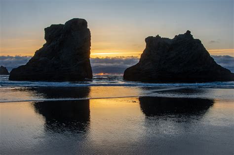오레곤의 밴든 해변에서 바다 뒤의 일몰 역광이 비추는 바다 스택이 해변의 물에 반사되고 장시간 노출은 파도의 움직임을 흐리게 합니다 0명에 대한 스톡 사진 및 기타 이미지