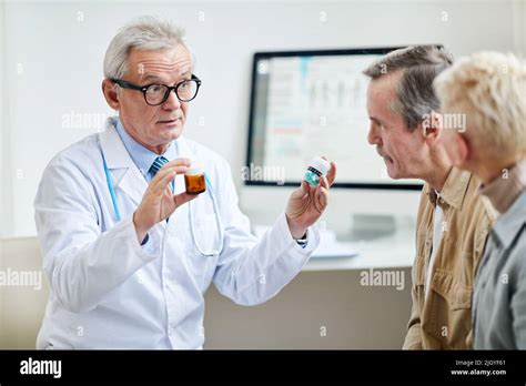 Confident Handsome Aged Physician In Lab Coat And Glasses Holding Two