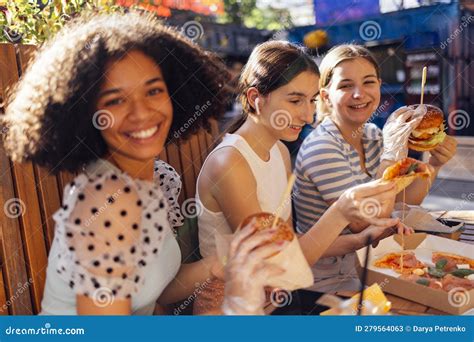 Cute Smiling Teenage Girls Are Sitting In Open Air Cafe And Eating Fast