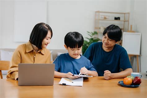 책상에서 숙제를 하는 아이들을 도와주는 부모들 아시아의 아들은 집에서 노트북에 숙제를 하고 있다 10 11세에 대한 스톡 사진