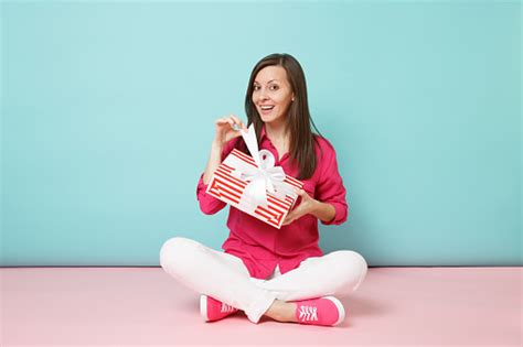 전체 길이 세로 여자 흰 장미 셔츠 블라우스에 밝은 핑크 블루 파스텔 벽 배경 스튜디오에 절연 층 보류 현재 상자에 앉아 바지 패션 라이프 스타일 개념입니다 복사 공간을