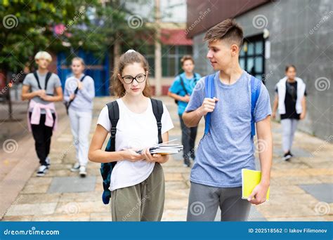 Студенты с рюкзаками и тетрадями идут вниз по улице Стоковое Фото изображение насчитывающей
