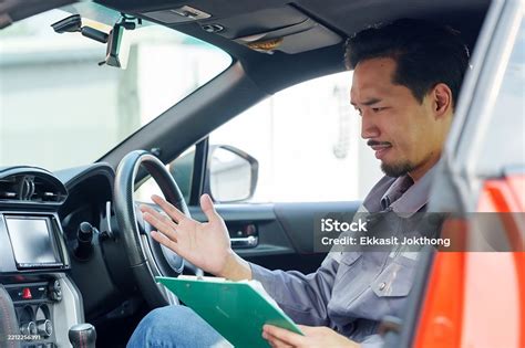 회색 유니폼을 입고 차실 안에 앉아 있는 아시아 성인 남성 정비사가 검사 보고서에 좌절한 표정을 지으며 일광 작업장에서 차량 유지 보수 문제에 대한 스트레스를 표현합니다