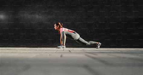 스포츠웨어에 맞는 매력적인 백인 갈색 머리와 포니 테일 스트레칭 다리의 측면보기 배경에는 어두운 벽이 있습니다 사진 Unsplash의 세르비아 이미지