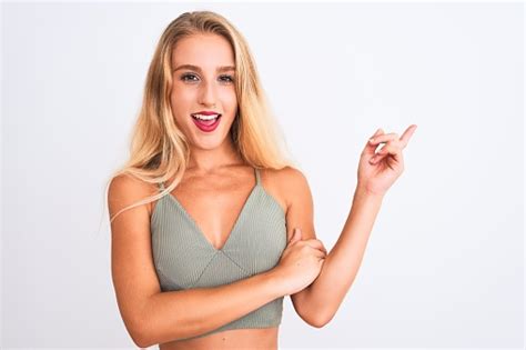 고립된 흰색 배경 위에 서있는 캐주얼 한 녹색 티셔츠를 입은 젊은 아름다운 여성은 얼굴에 큰 미소를 지으며 카메라를 바라보는 옆구리를 손가락으로 가리킵니다 T 셔츠에 대한