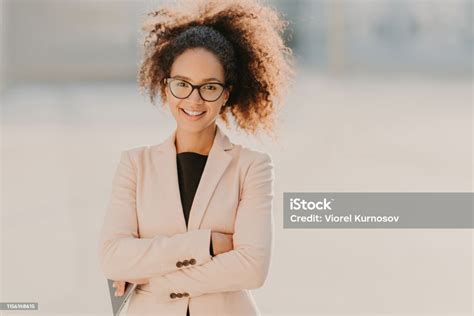 곱슬 한 아프로 머리와 자신감 쾌활한 여성 기업가 팔을 접힌 유지 현대 태블릿 컴퓨터를 사용 긍정적으로 미소 비즈니스 파트너