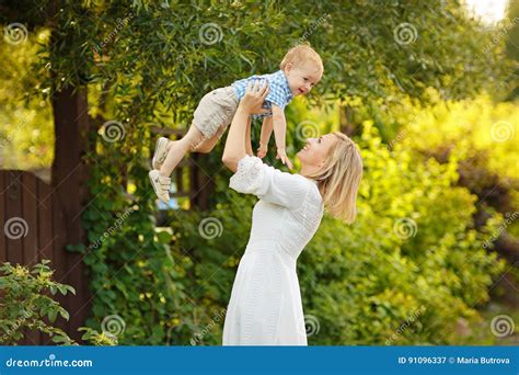 Mom Blonde In White Dress Lifts Up The Little Boy And Laughing A Stock