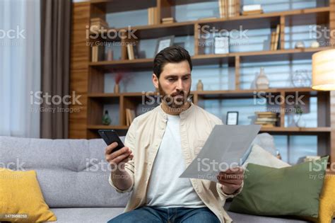 걱정스러운 청년이 집 소파에 앉아 전화와 문서 편지를 들고 있습니다 계약 계정 신용 확인 35 39세에 대한 스톡 사진 및 기타 이미지 Istock