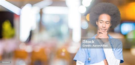 손으로 턱 질문 잠겨있는 표현에 대 한 생각에 아프로 머리를 가진 젊은 아프리카계 미국인 의사 남자 사려깊은 얼굴 미소 의심 개념입니다 건강관리와 의술에 대한 스톡 사진 및