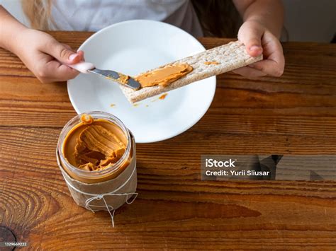 나무 테이블 홈 키친에 땅콩 버터와 바삭바삭한 빵을 먹는 아이 빵 슬라이스 통곡물 간식을 곁들인 여학생 땅콩버터에 대한 스톡 사진 및 기타 이미지 Istock