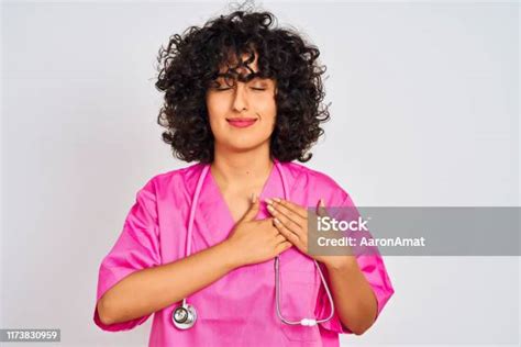 고립 된 흰색 배경 위에 청진기를 입고 곱슬 머리를 가진 젊은 아랍 의사 여성은 닫힌 눈과 얼굴에 감사 제스처로 가슴에 손을 미소 짓고 있습니다 건강 개념 감사에 대한 스톡