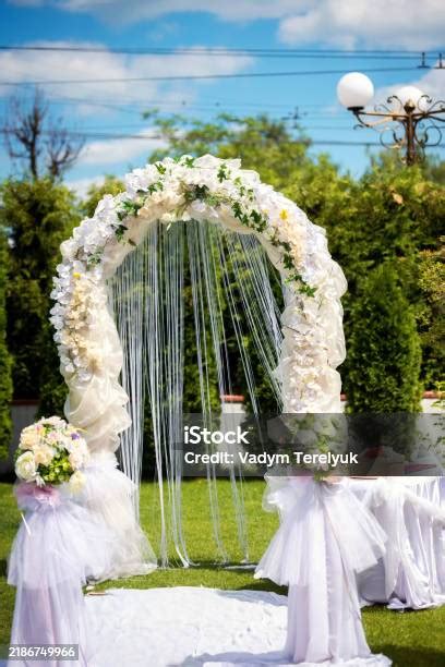 야외 환경에서 드레이핑 패브릭이 있는 우아한 꽃 결혼식 아치 햇볕이 잘 드는 야외에서 꽃과 커튼으로 장식된 아름다운 결혼식 아치 0명에 대한 스톡 사진 및 기타 이미지
