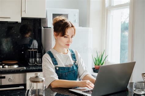 Remote Work At Home Concentrated Young Woman Working On Laptop At The Kitchen Table In Tiny