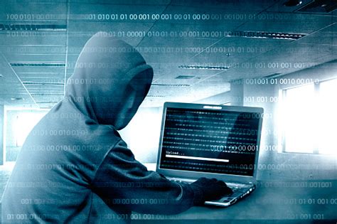 Hacker In Black Hoodie Using Laptop On The Desk To Hacking System With