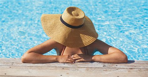 모자를 쓴 아름다운 여자는 물 속의 수영장 나무 부두에서 휴식을 취하고 열대 리조트에서 여름 휴가를 즐기고 있습니다 수영장 가장자리에서 일광욕을 하는 날씬한 젊은 여성