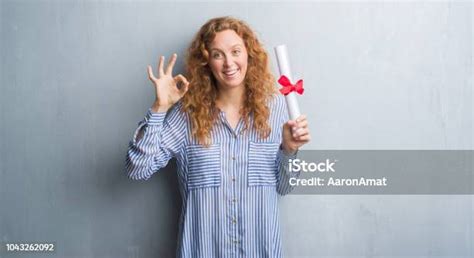 손가락 우수한 기호 확인 표시를 하 고 졸업장을 들고 회색 그런 지 벽에 빨강 머리 젊은 비즈니스 우먼 개념에 대한 스톡 사진