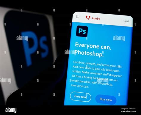 Person Holding Cellphone With Webpage Of Graphics Editor Software Adobe Photoshop On Screen In
