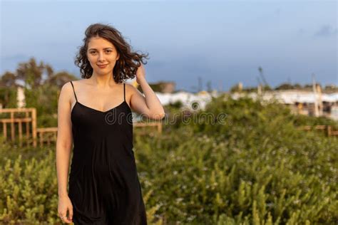 Jovencita De La Morena Con El Pelo Largo Y Rizado En Un Corto Vestido Negro Con Patas Mojadas Se