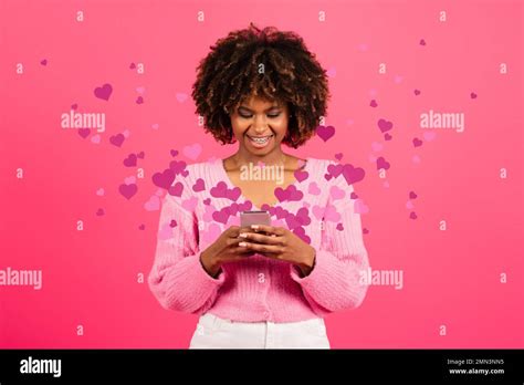 Glad Young Black Curly Lady With Braces Typing On Phone With Many Hearts Reading Message Stock