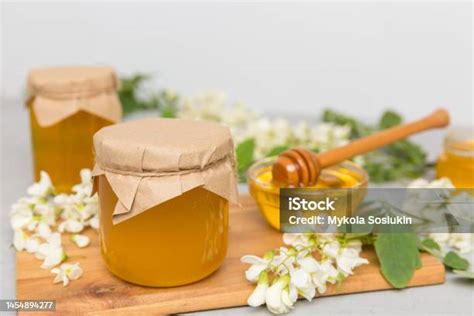 달콤한 꿀 항아리가 봄 아카시아 꽃을 둘러싸고 있습니다 꿀은 항아리에있는 숟가락에서 흐릅니다 나무 배경에 맑은 신선한 아카시아 꿀 항아리 1위에 대한 스톡 사진 및 기타