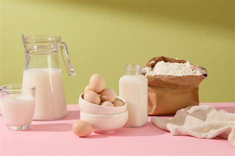 유리잔과 병에 우유 계란 몇 개 파스텔 그린 배경에 분홍색 테이블에 밀가루를 곁들인 맛있는 수제 케이크를 위한 신선한 재료 복사 공간이 있는 앞면 보기 건강한 식생활에 대한