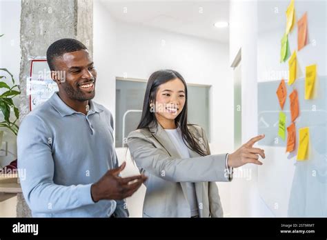 Smiling Businesspeople Analyzing Project Plan Using Colorful Sticky Notes On Whiteboard In