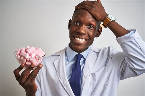 고립 된 흰색 배경 위에 마시멜로와 그릇을 들고 아프리카 계 미국인 의사 남자 머리에 손으로 스트레스 수치와 깜짝 얼굴 분노와 좌절에 충격 실수에 대한 두려움과 화가 감정에