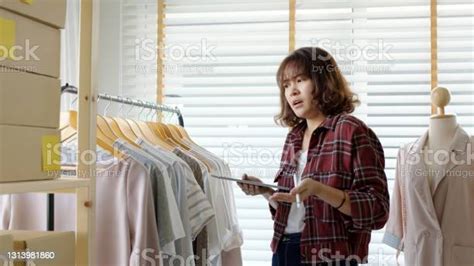 젊은 매력적인 아름다운 힙스터 아시아 여성 패션 스토어 소유자는 홈 오피스 작은 중소기업 기업가 전자 상거래 개념에서 철도 랙에 디지털 태블릿 체크 스톡 옷이나 패키지