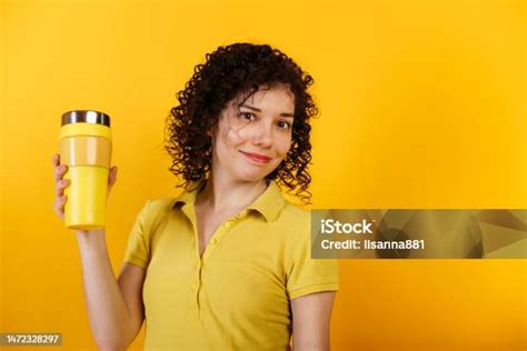 웃는 젊은 여자는 커피나 차와 함께 열 머그잔을 들고 있다 밝은 빨간 셔츠와 노란색 티셔츠를 입은 곱슬 소녀 여성 손에 제로 웨이크 테이크 아웃 커피 컵 노란색 배경에 격리