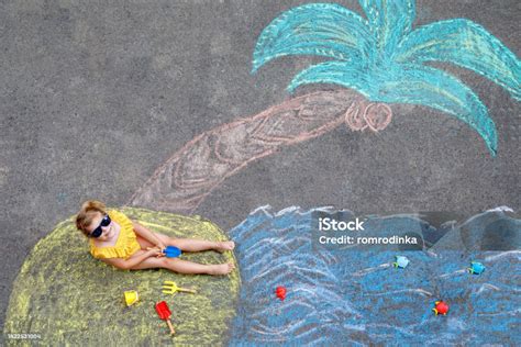 바다 모래 아스팔트에 화려한 분필로 칠해진 손바닥으로 수영복을 입은 행복한 어린 미취학 소녀 분필 그림으로 재미있게 지내는