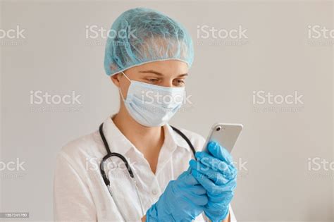 의료복을 입은 집중여성 의사 나 간호사의 실내 샷 목에 청진기로 포즈를 취하고 휴대 전화를 사용하여 전자 메일 이나 전자 환자의 의료 카드를 확인합니다 간호사에 대한 스톡