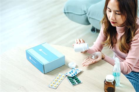 젊은 아시아 여성은 아프고 피곤하며 집에있는 거실에서 약을 복용 한 후 파란색 직물 소파와 담요에 앉아서 휴식을 취합니다 여자는 Phamacy 응급 처치 키트 상자를