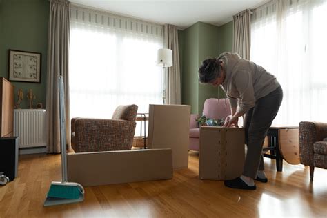 텅 빈 아파트 방에 혼자 있는 활동적인 선배 여성이 골판지 상자에서 짐을 풀고 집을 옮기는 동안 50 54세에 대한 스톡 사진 및 기타 이미지 Istock