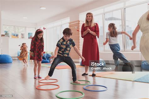 작은 보육원 아이들 교실에서 실내 바닥에 여성 교사와 함께 운동을하고 훌라 후프 서클을 뛰어 넘으면 바닥에서 추적됩니다 아이에