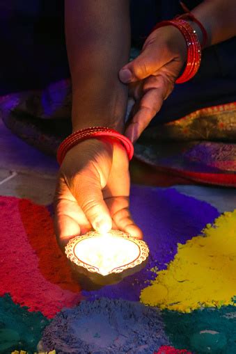 갈랄 랑골리 디자인 레드 퍼플 옐로우 및 그린 파우더 페인트 꽃잎 패턴 어두운 불꽃 빛의 디왈리 축제의 중심에 조명 디야 를 배치 인식 할 수없는 사람의 클로즈업 이미지
