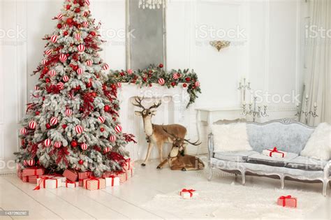 빛나는 화환과 선물이 있는 크리스마스 트리 세련된 흰색 거실 인테리어에는 크리스마스 트리 벽난로 베개가 있는 소파가 있습니다 집에서 크리스마스 새해 겨울 가정 장식