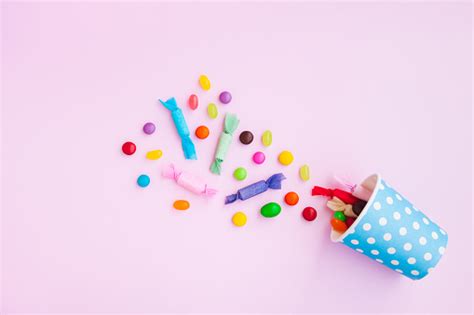 분홍색 배경에 하얀 점이 있는 파란 종이컵에서 나온 다양한 종류의 다채로운 사탕 다양한 사탕 개체 그룹에 대한 스톡 사진 및 기타 이미지 Istock