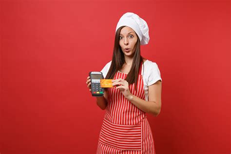 주부 여성 요리사 요리사 또는 줄무늬 앞치마 T셔츠 모자 요리사 모자 빨간 벽 배경에 고립 된 베이커 여자 잡고 손에 은행 결제 터미널 신용 카드 Nfc 장치 모의 복사