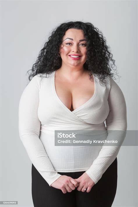 곱슬 어두운 머리를 가진 아름다운 플러스 크기의 여자 잘 생긴 과체중 소녀는 쾌활한 이빨 미소와 스튜디오에서 포즈를 취하고 있습니다 갈색 머리에 대한 스톡 사진 및 기타