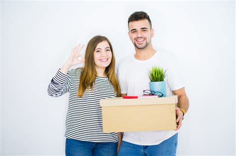 손가락으로 확인 기호를하고 흰색 고립 된 배경을 통해 새로운 가정으로 이동 골판지 상자를 들고 젊은 부부 우수한 기호 2명에 대한 스톡 사진 및 기타 이미지 Istock