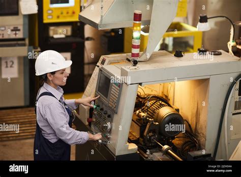 serious busy female technical engineer standing at cnc lathe and pushing buttons while choosing