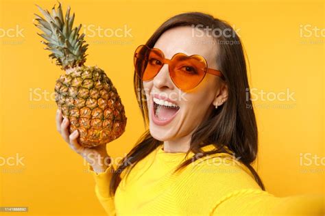 심장 안경에 쾌활 한 젊은 여자의 Selfie 샷을 닫습니다 노란 오렌지 배경에 고립 된 신선한 잘 익은 파인애플 과일을 개최 합니다 사람들은 생생한 라이프 스타일 휴식