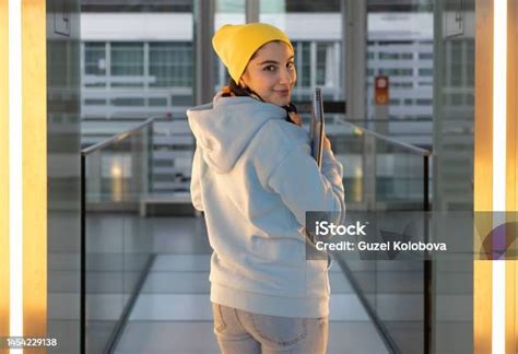 파란색 스웨트셔츠와 노란색 모자를 쓴 웃는 여학생이 유리 복도를 따라 걷는다 캠퍼스에 대한 스톡 사진 및 기타 이미지 캠퍼스 18 19세 건물의 층 Istock