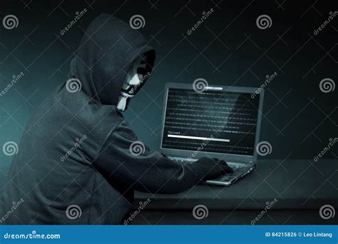Hooded Hacker With Anonymous Mask Using Laptop To Steal Data Editorial