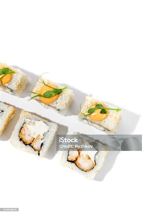 바깥쪽에 참깨를 곁들인 마키 초밥 매운 소스와 마이크로 그린을 얹은 튀김 새우 하얀 배경에 고립된 매운 새우 마키 롤 바삭한 새우와 딱딱한 그림자가 있는 트렌디 한 스시 롤