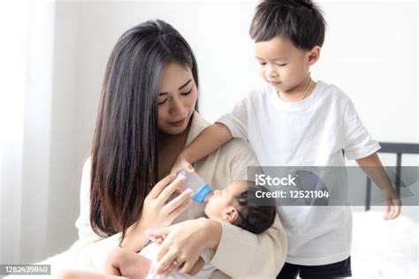 젊은 아시아 어머니는 귀여운 신생아를 껴안고 아들 흰색 침실로 우유 양식 병을 먹이 자녀를 양육하는 아내의 의무 어머니와 자식 개념 18 23 개월에 대한 스톡 사진 및