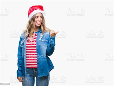 아름 다운 젊은 금발 여자 생기고 엄지 측면 가리키는 행복 한 얼굴로 웃 고 고립 된 배경 위에 크리스마스 모자를 쓰고 가리키기에 대한 스톡 사진 및 기타 이미지 Istock