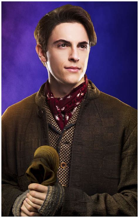 A Man In A Brown Sweater And Red Scarf Holding A Hat With His Hands On His Chest